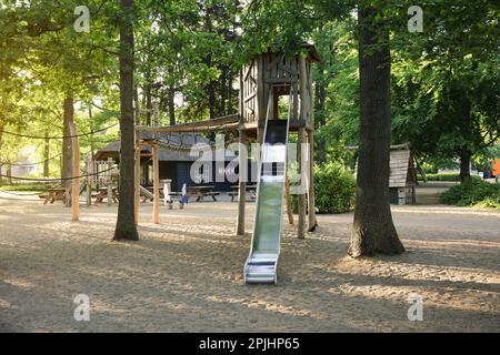 Wooden slide with bridge near big trees in park. Outdoor playground ...