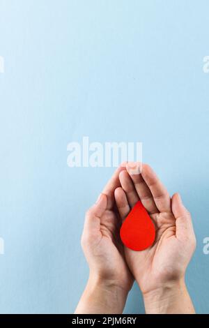 Hands of caucasian woman cupping blood drop on blue background with ...