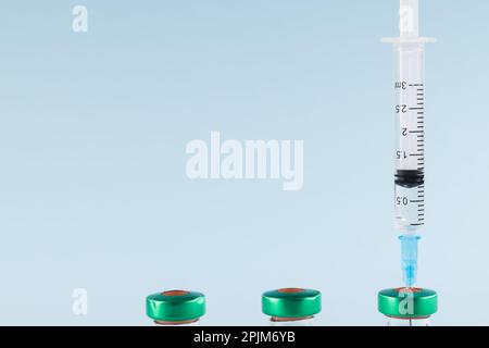 Three vials with syringe filling from one, on blue background with copy ...