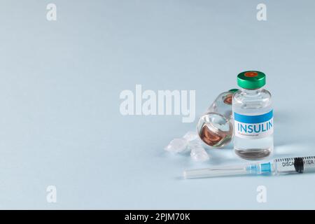 Vials of insulin with caplets and syringe on blue background with copy ...
