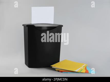 Shredder with sheet of paper and colorful folders on grey background ...