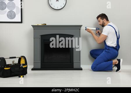 Professional technician sealing electric fireplace near white wall in ...