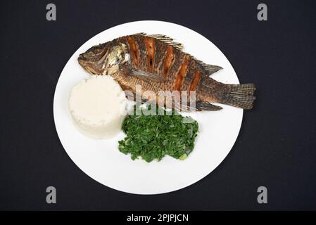 Grilled fish served with ugali and vegetables on an isolated background ...