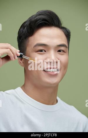 Young man using serum for skin care on white background Stock Photo - Alamy