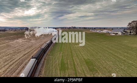 A vintage steam locomotive is chugging along a railway track, emitting ...
