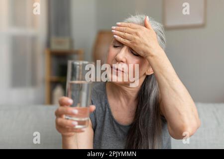 Menopause. Woman with glass of water suffering from heat flash at ...