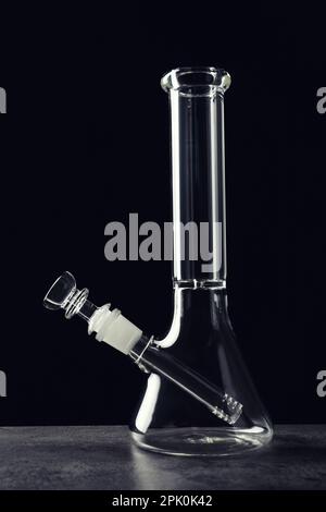 Glass bong on grey table against black background, space for text ...