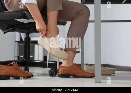 Woman taking off uncomfortable shoes and putting on sneakers in office ...