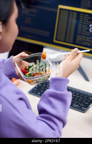 closeup of a young software developer eating a fruit salad from a clear ...