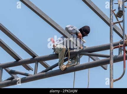 A welder is welding steel on a steel roof truss. Working at height ...