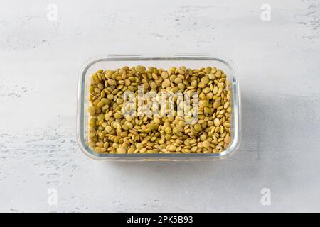 Raw soaked lentils in glass food container on light gray background ...