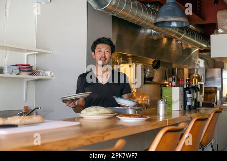 A chef working in a restaurant, at the pass preparing plates of food ...