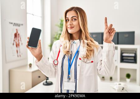Surprised female doctor, pointing at smartphone app screen, standing ...