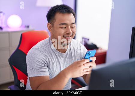 Young chinese man streamer using computer and smartphone at gaming room ...