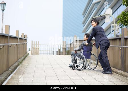 Man in suit pushing man in wheelchair Stock Photo - Alamy