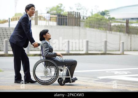 Man in suit pushing man in wheelchair Stock Photo - Alamy