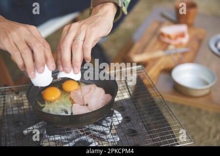 Man dropping an egg in a frying pan outdoors Stock Photo - Alamy