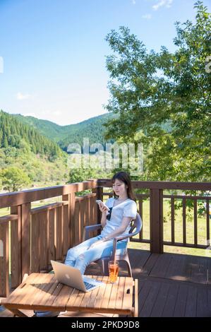 Woman working remotely from a log cabin balcony Stock Photo - Alamy