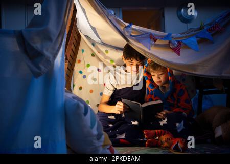Brothers reading a book in a tent made of sheets Stock Photo - Alamy