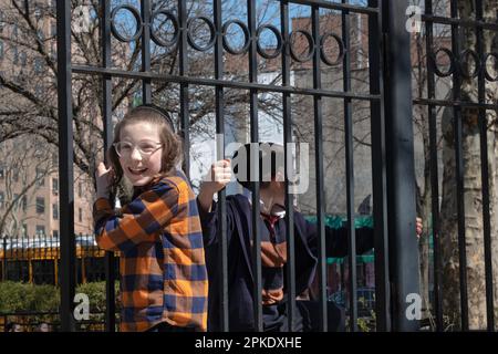 A Hasidic Jewish boy enjoys swinging on a fence door during recess from ...