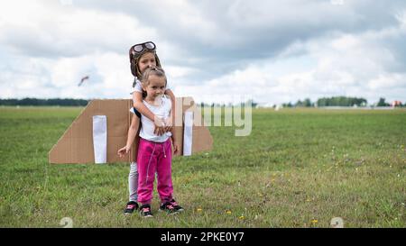Two little girls in pilot's costumes are hugging in the field by the ...