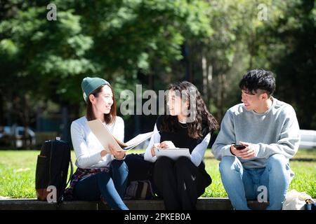 Three students talking outside with notebooks spread out Stock Photo ...
