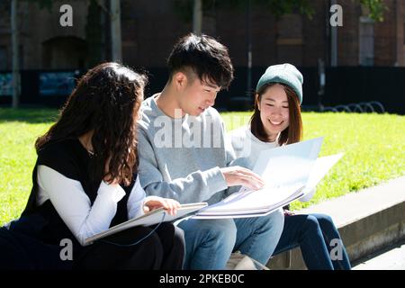 Three students talking outside with notebooks spread out Stock Photo ...
