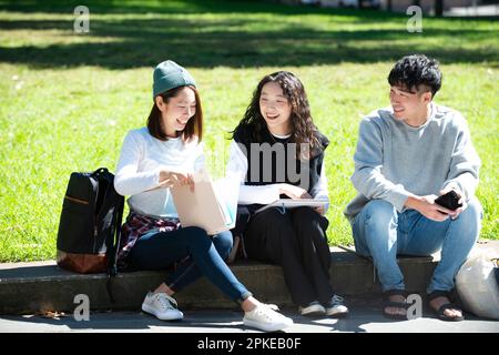 Three students talking outside with notebooks spread out Stock Photo ...