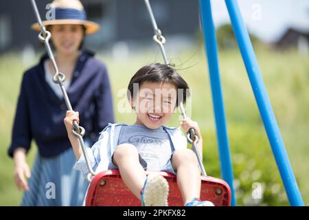 Boy being pushed on the swing by his mother Stock Photo - Alamy