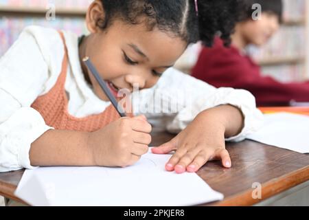 Cute pupils writing and painting on paper at desk in classroom Stock ...