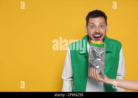 Woman offering tasty potato chips to excited man on orange background ...