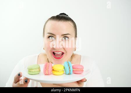 satisfied and happy woman eating macaroons on white background space ...