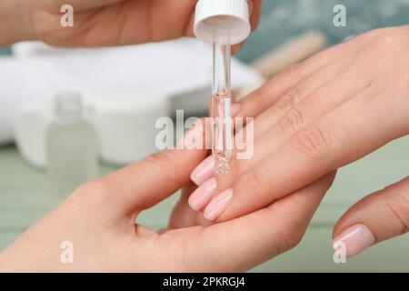 Manicure master applying cuticle oil onto female fingernails on light ...