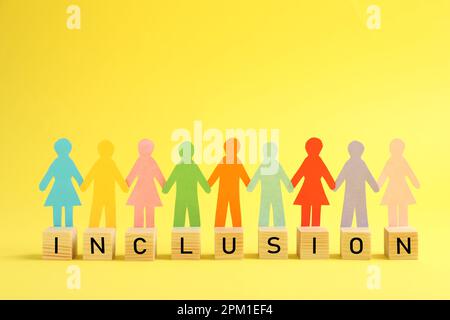 Paper human figures with wooden cubes on yellow background. Diversity ...