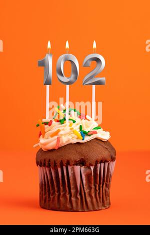 Birthday cake with number 102 candle - Sparkling orange background with ...