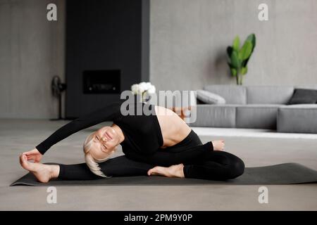 A young slim woman has done splits, and is stretching herself with her ...