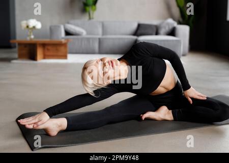 A young slim woman has done splits, and is stretching herself with her ...