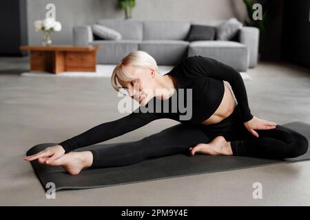 A young slim woman has done splits, and is stretching herself with her ...