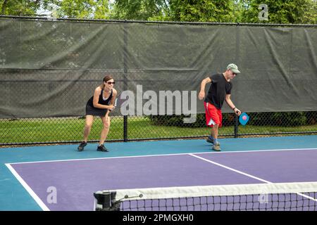 A pickleball player serves while her partner prepares for a return on a ...