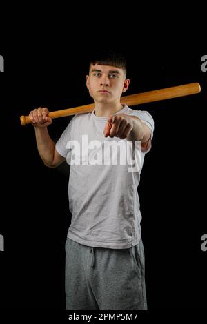 A teenage boy with a basball bat and pointing against a black ...