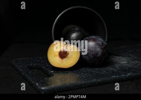 Cut plum showing an open half with fruitstone on a black countertop ...