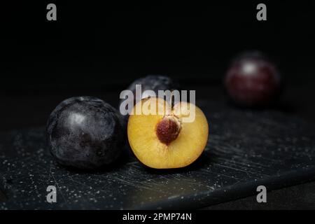Cut plum showing an open half with a fruitstone on a black countertop ...