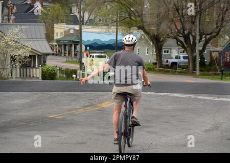A senior man riding a bicycle signals a left turn as he rides along a ...