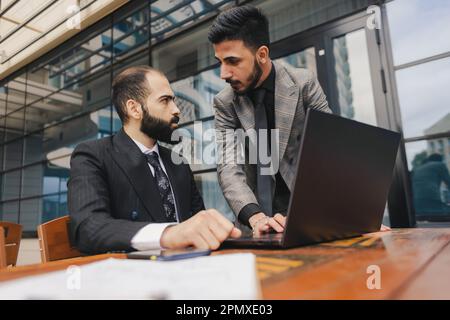 business people meets outdoors. Two men are using a laptop. Working ...
