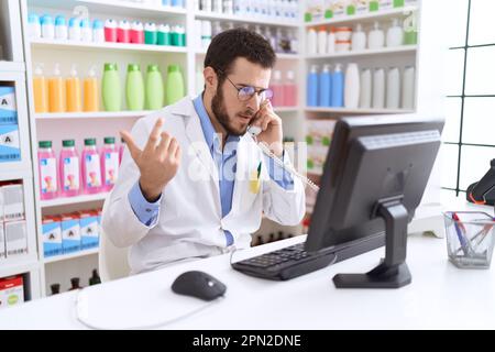 Young hispanic man pharmacist talking on telephone using computer at ...