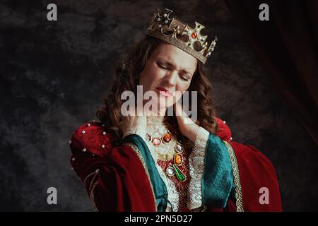 stressed medieval queen in red dress with crown having neck pain on ...