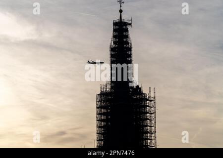 A plane flying very close to a building under construction. Sun rising ...