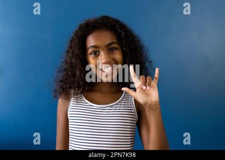 Portrait of biracial girl using sign language with hand on blue ...