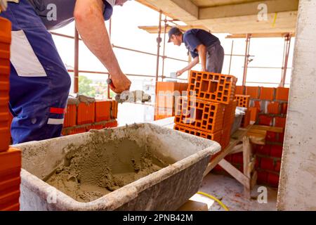 Mason, bricklayer worker grabs mortar from the plastic trough with ...