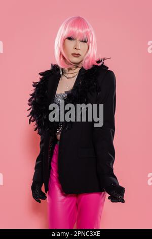 Drag queen in jacket and gloves touching sunglasses on pink background ...